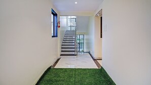Um corredor com escadaria de mármore, um extintor de incêndio e uma pequena janela.