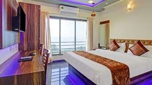 Quarto de hotel com uma cama grande, uma escrivaninha com controle remoto, ar condicionado e vista para o exterior.