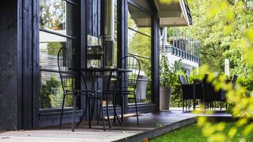Uma área de estar moderna ao ar livre, com mesa, cadeiras, janelas amplas e vista para o verde.