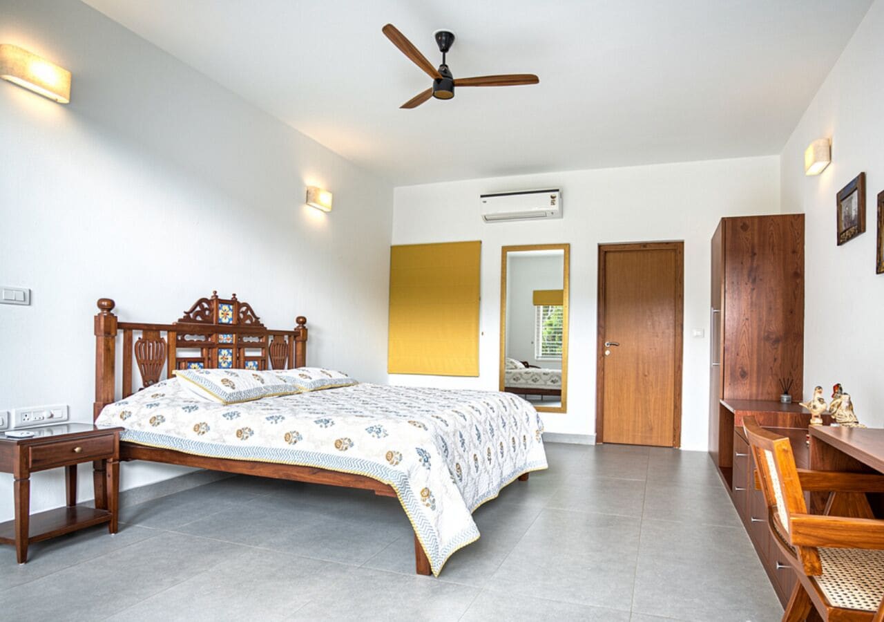 Quarto com cama de madeira, mesas de cabeceira, ventoinha no teto, aparelho de ar condicionado e guarda-roupa de madeira.