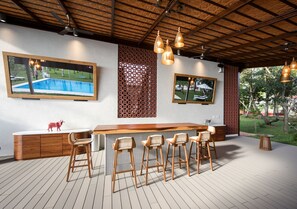 Uma área de bar com balcão de madeira, banquetas e iluminação pendente.
