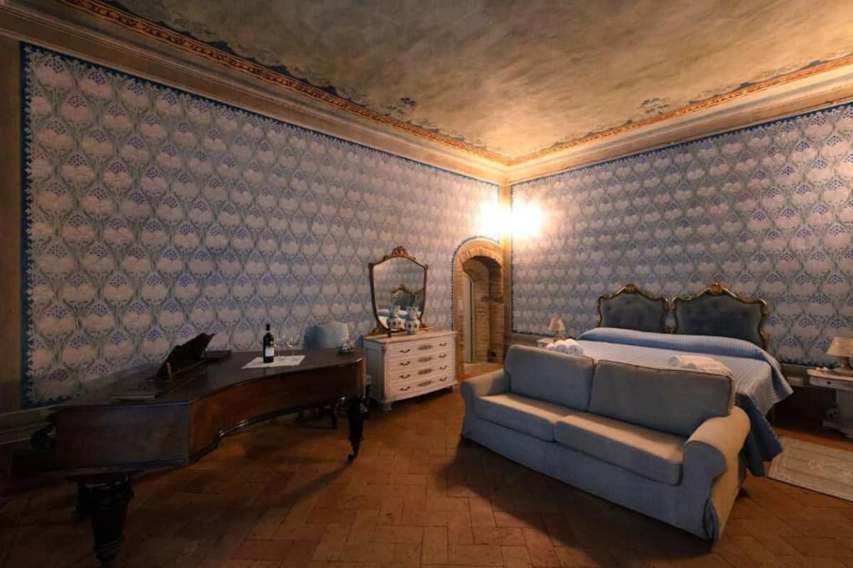 Um quarto com papel de parede estampado, uma cama, uma cômoda, um espelho e uma escrivaninha com uma cadeira.