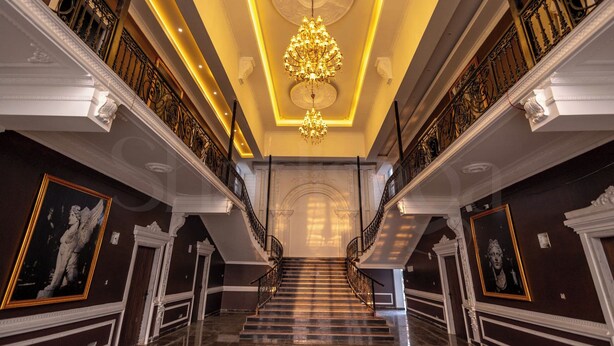 Uma escadaria imponente com grades ornamentadas, um lustre e obras de arte emolduradas nas paredes.