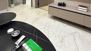 Quarto de hotel moderno com televisão de tela plana, sofá, mesa de centro, controle remoto e uma planta.