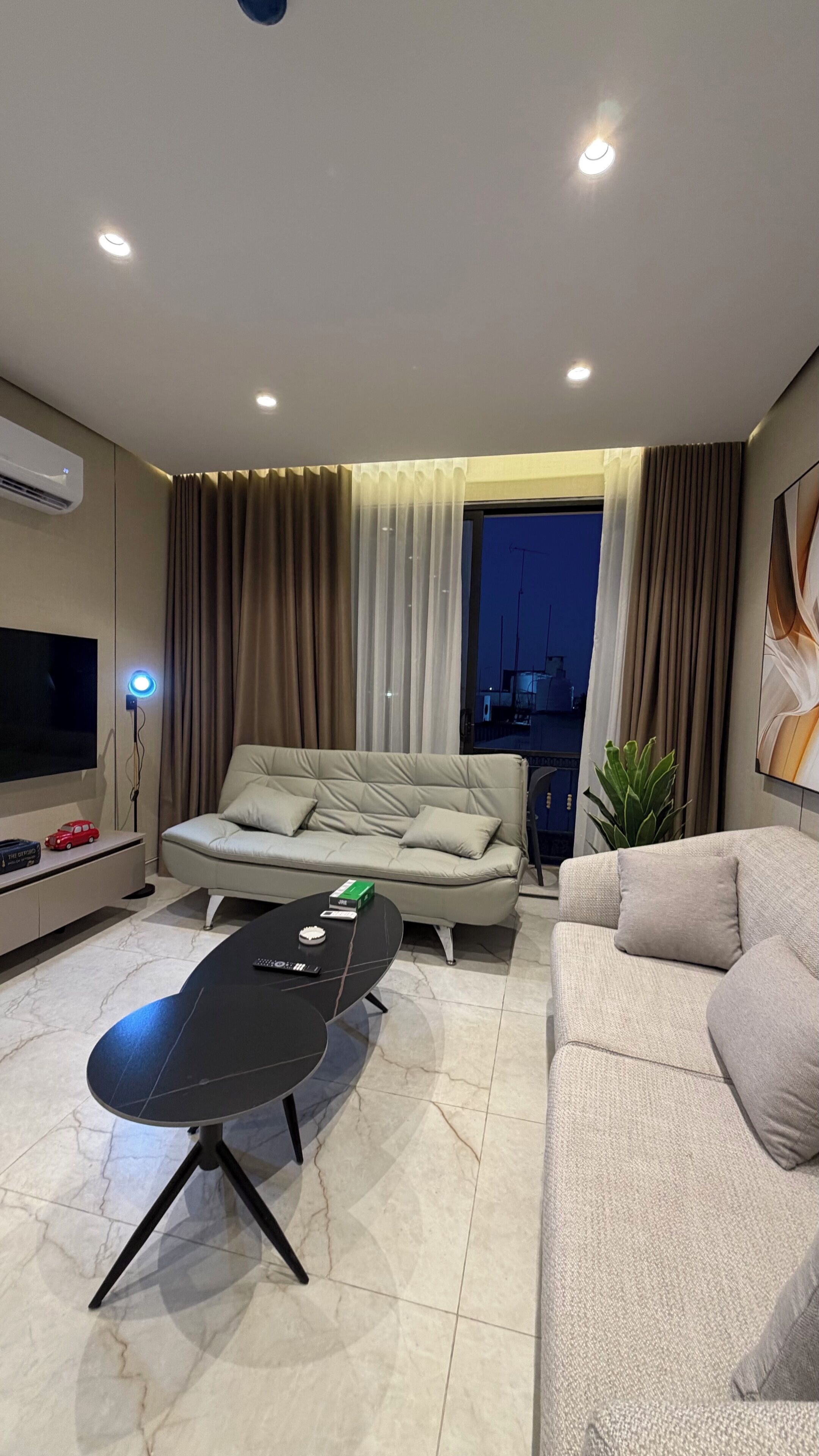 Uma sala de estar moderna com sofá, mesa de centro, TV e vista para uma varanda.