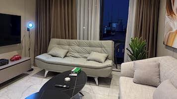 Uma sala de estar moderna com sofá, mesa de centro, TV e vista para uma varanda.