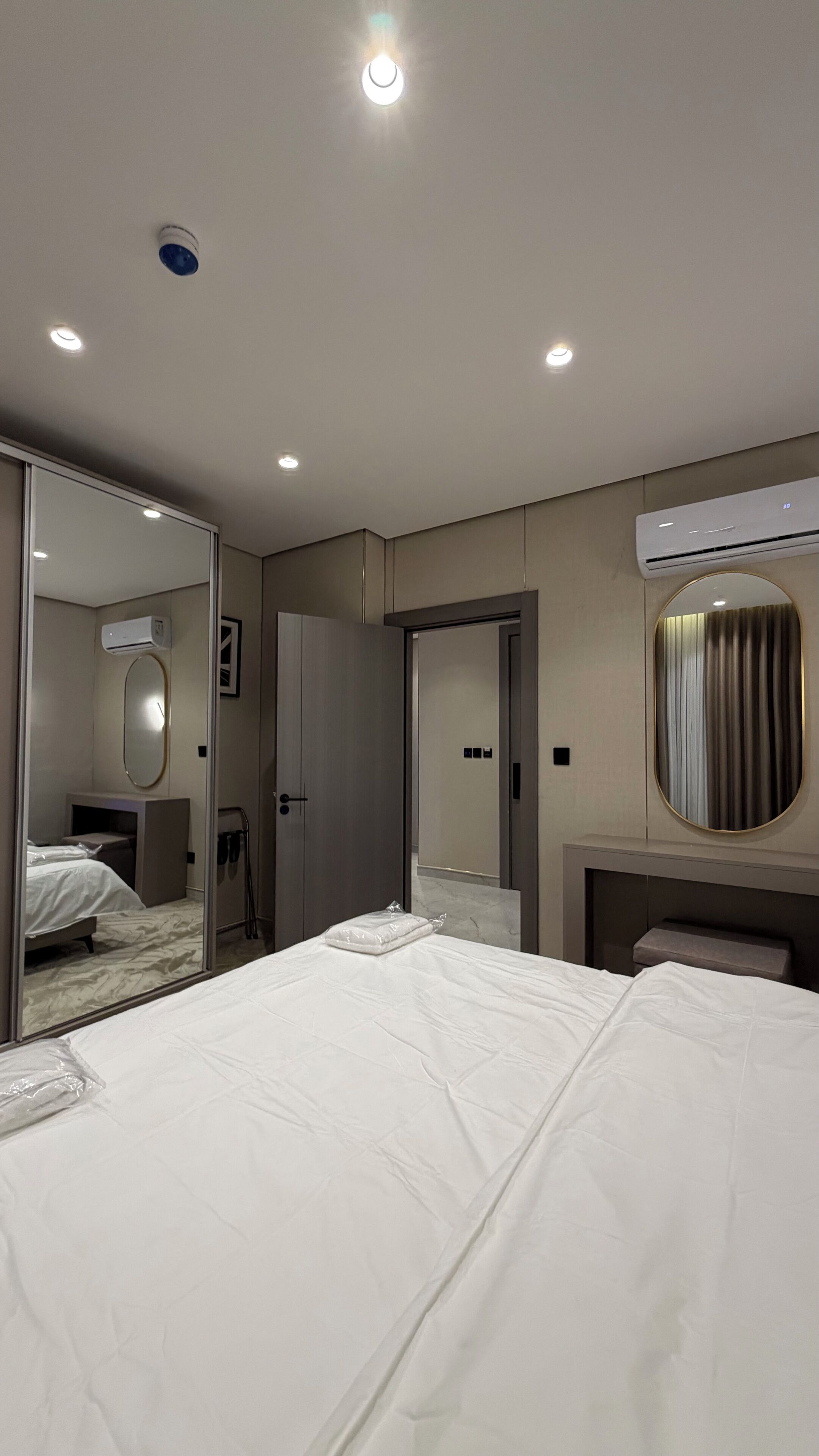 Quarto de hotel com cama, espelho, ar condicionado e porta.
