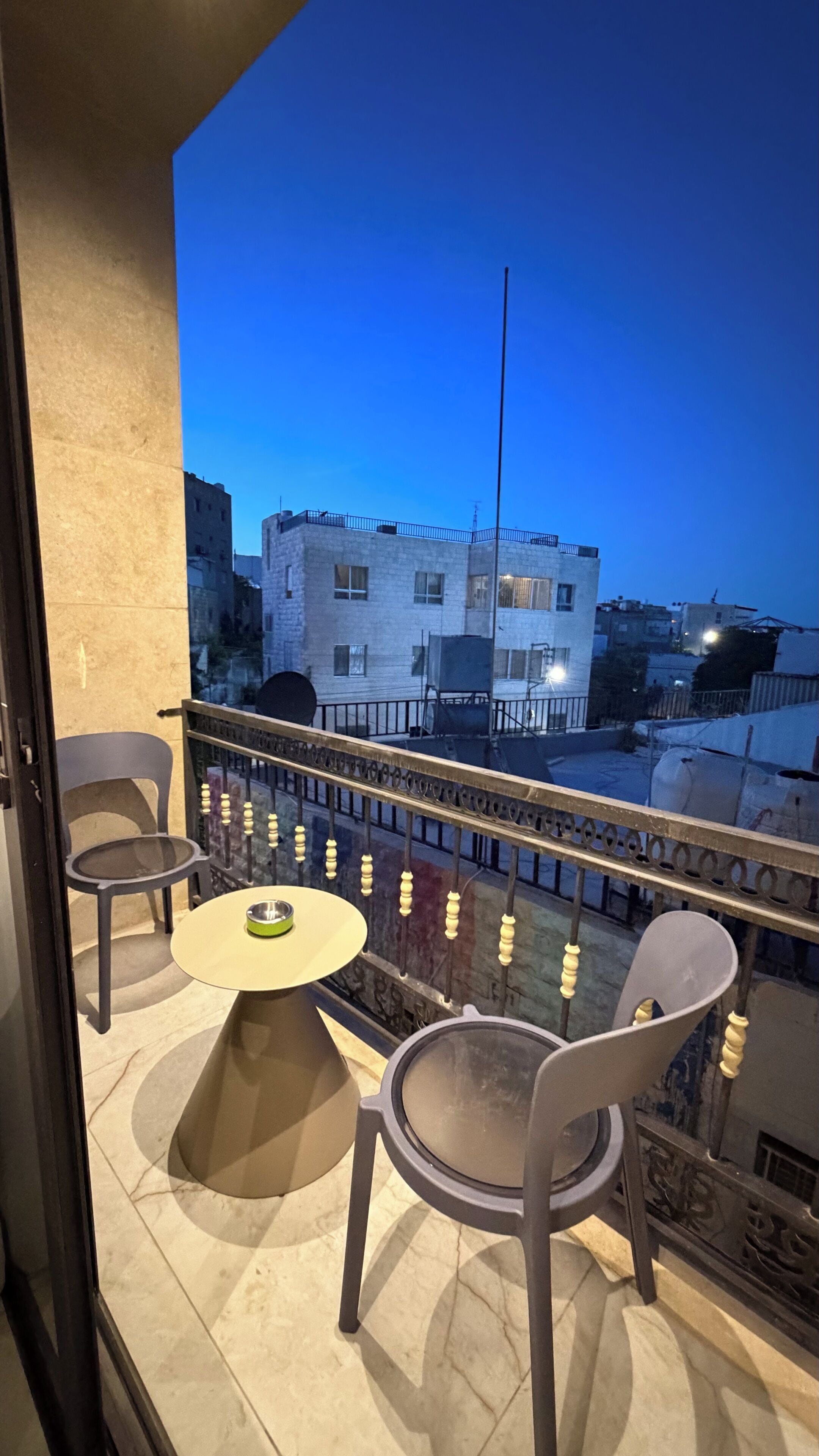 Varanda com mesa e duas cadeiras, vista para edifícios e céu limpo.