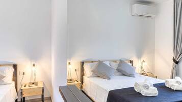 Quarto de hotel com cama, mesas de cabeceira, um banco, ar condicionado e toalhas.