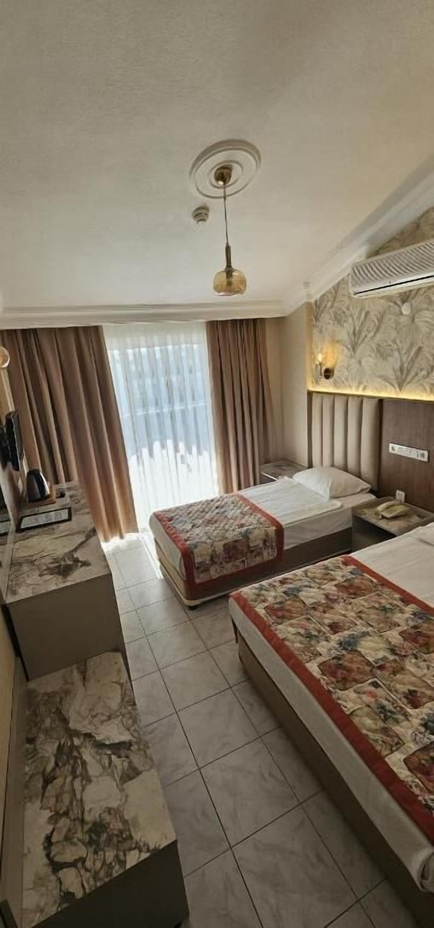 Quarto de hotel com duas camas, uma escrivaninha, uma cadeira, uma máquina de café e janela com cortinas.