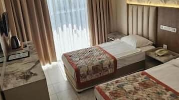 Quarto de hotel com duas camas, uma escrivaninha, uma cadeira, uma máquina de café e janela com cortinas.