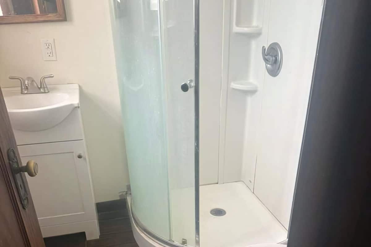 Uma casa de banho com cabine de chuveiro em vidro, sanita, lavatório e espelho.
