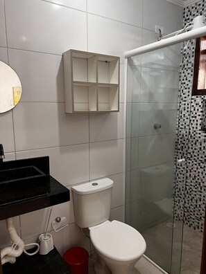 Uma casa de banho com sanita, lavatório, chuveiro e espelho.
