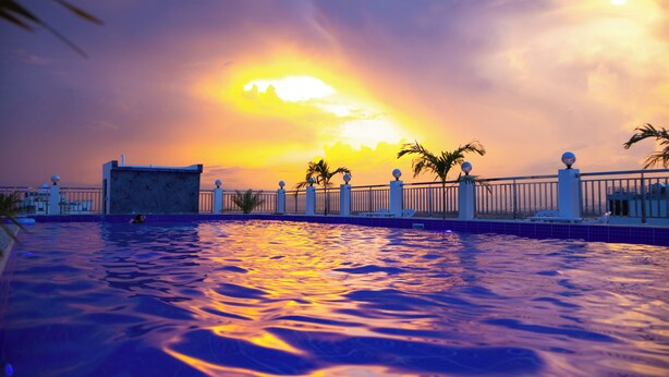 Piscina com vista para o pôr do sol, palmeiras e uma cerca.