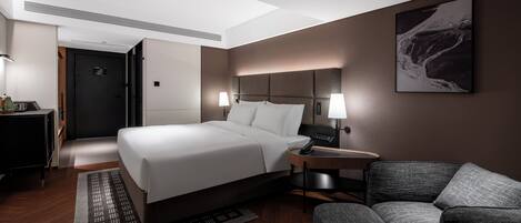 Quarto de hotel moderno com cama, mesa de cabeceira, luminária e uma cadeira.
