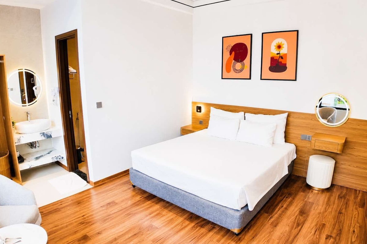 Quarto de hotel com cama, mesa de cabeceira, espelho, luminária na parede e duas imagens emolduradas.