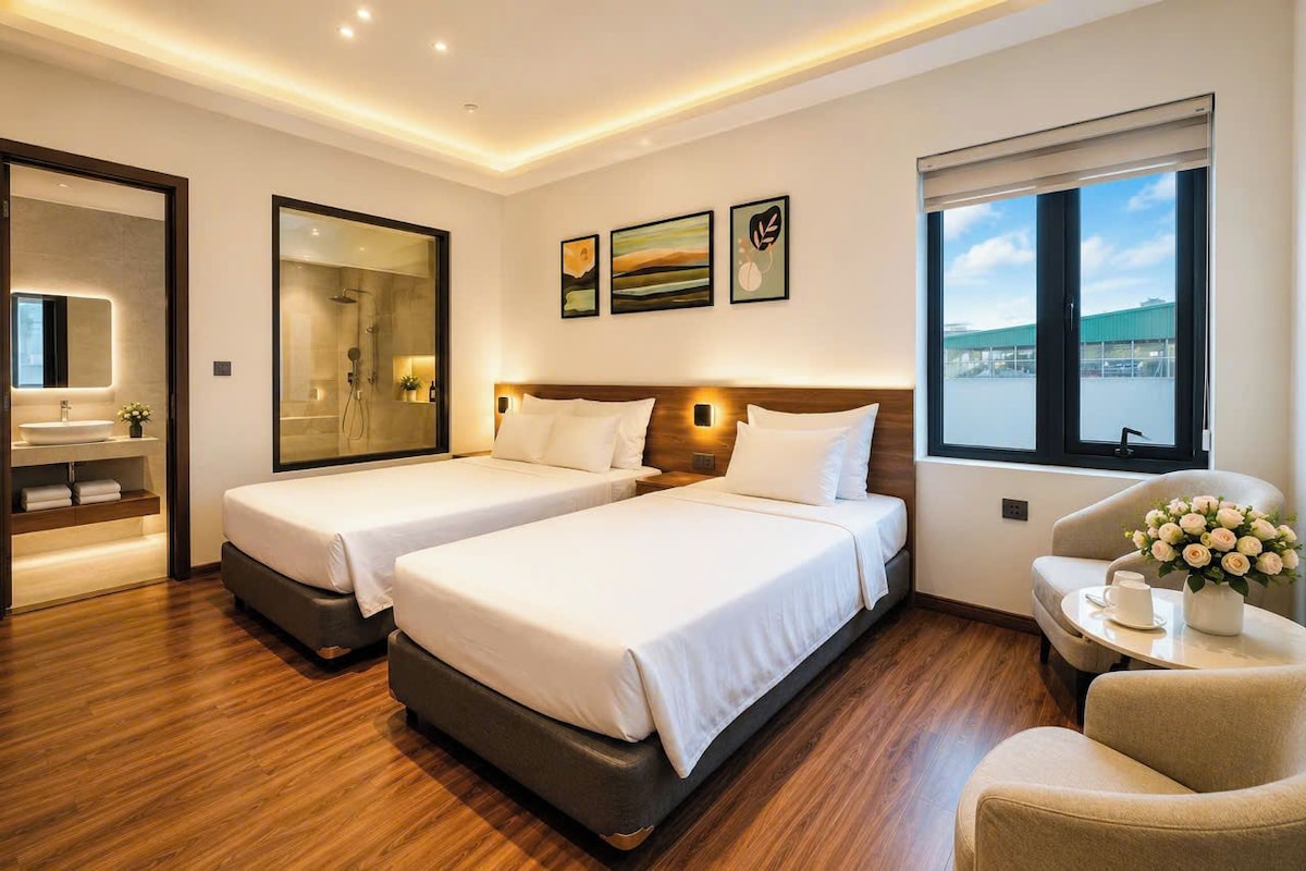 Quarto de hotel com duas camas, banheiro, janela com vista e obras de arte na parede.