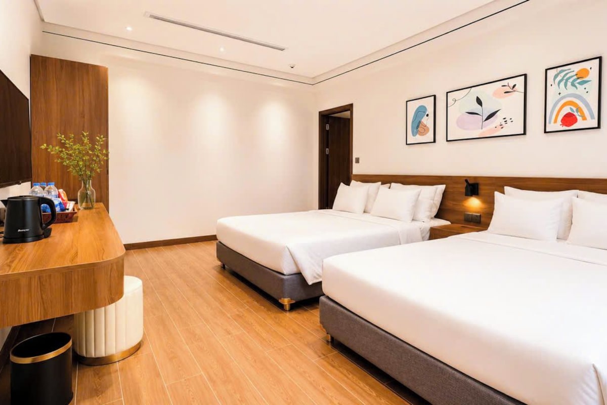 Quarto de hotel com duas camas, uma escrivaninha de madeira, televisão e obras de arte na parede.