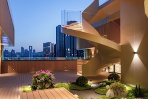 Um edifício moderno com varanda de vidro e vista para a cidade ao entardecer.