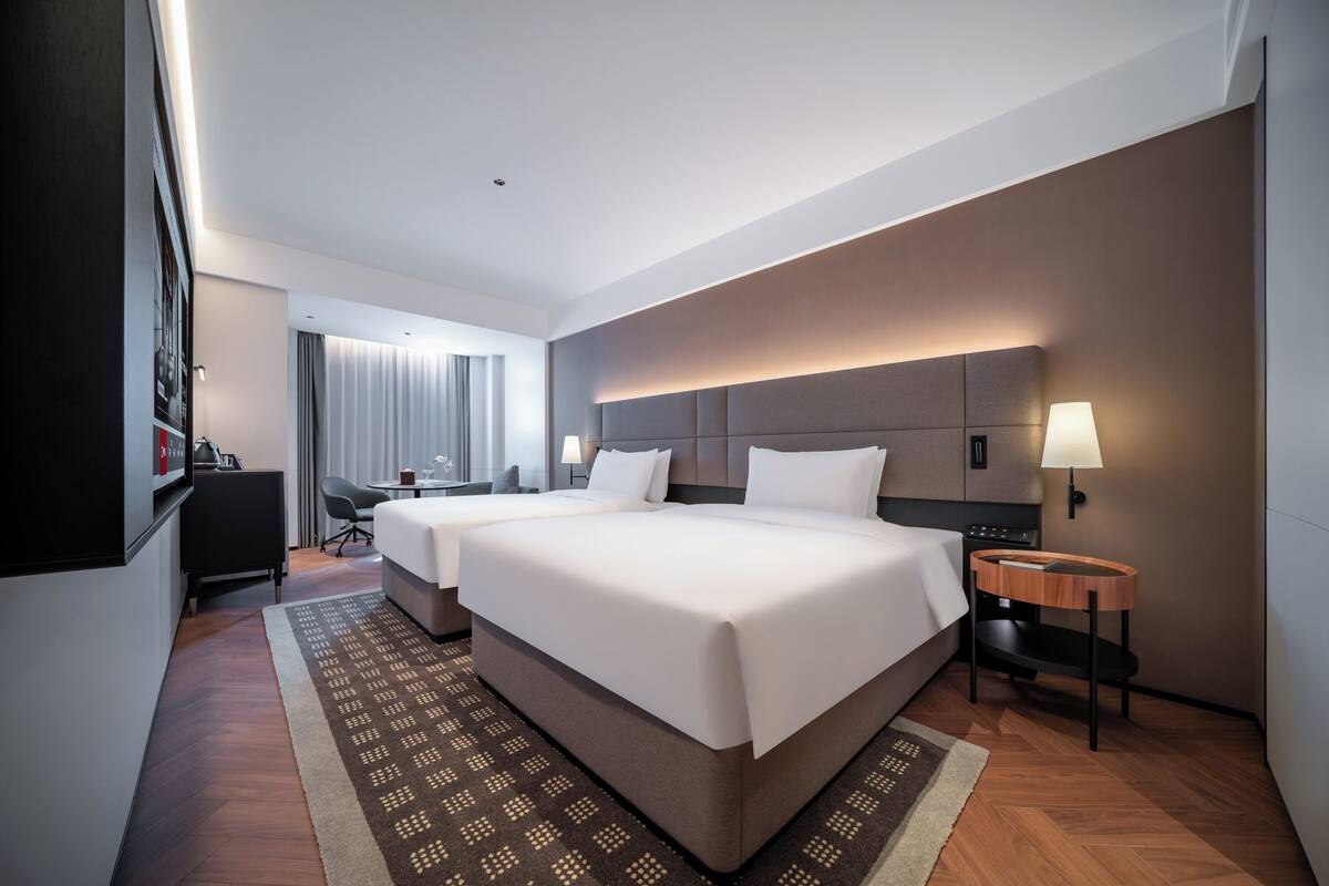 Quarto de hotel com uma cama grande, uma mesa, uma cadeira, um abajur e uma mesinha de apoio.