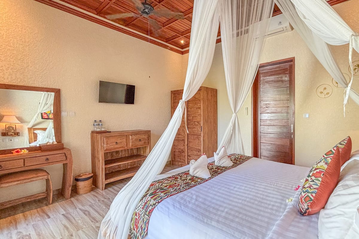Quarto com cama de dossel, móveis de madeira, espelho e televisão na parede.