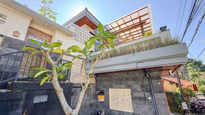 Um edifício residencial com fachada de pedra, uma varanda com guarda-corpo de madeira e uma pequena árvore na frente.