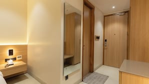Quarto de hotel com guarda-roupa de madeira, mesa de cabeceira com telefone, espelho e tapete pequeno.