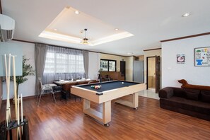 Uma mesa de bilhar em um ambiente com piso de madeira, área de refeições e um sofá.