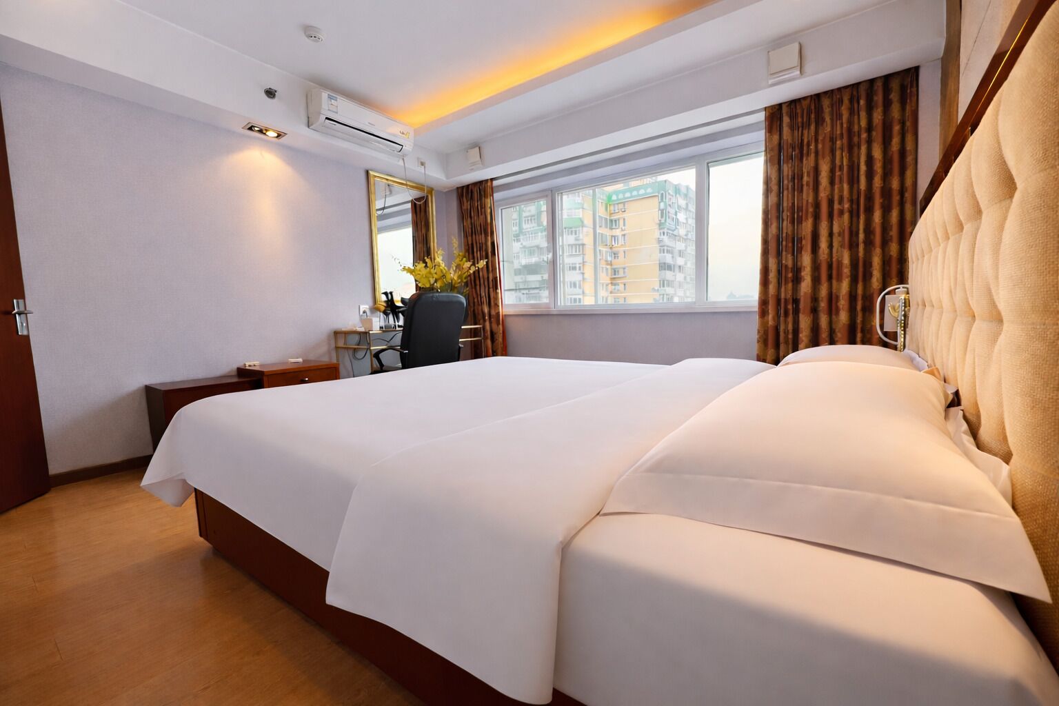 Quarto de hotel com uma cama grande, uma escrivaninha, uma cadeira e uma janela com cortinas.