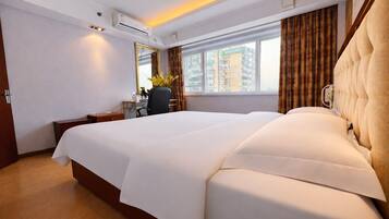 Quarto de hotel com uma cama grande, uma escrivaninha, uma cadeira e uma janela com cortinas.