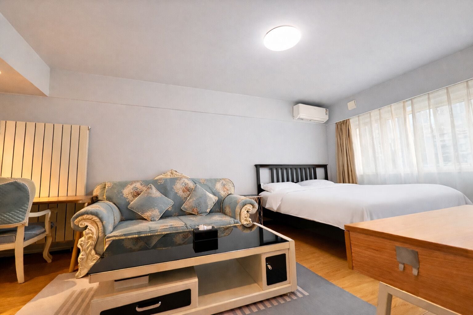 Quarto de hotel com cama, sofá, mesa pequena, cadeira e janela com cortinas.