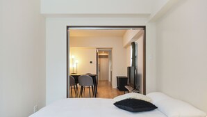 Quarto de hotel com cama, escrivaninha, cadeiras, televisão e abajur.