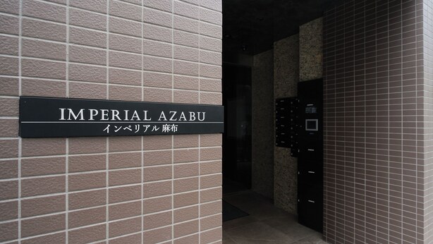 Um sinal com 'IMPERIAL AZABU' e texto japonês, uma parede com azulejos e uma porta que dá para um espaço com um armário preto.