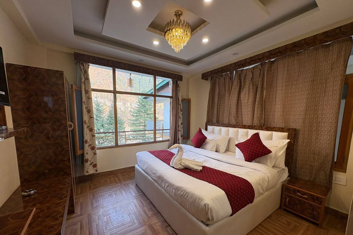 Quarto de hotel com cama grande, um candelabro, janela com vista e piso de madeira.