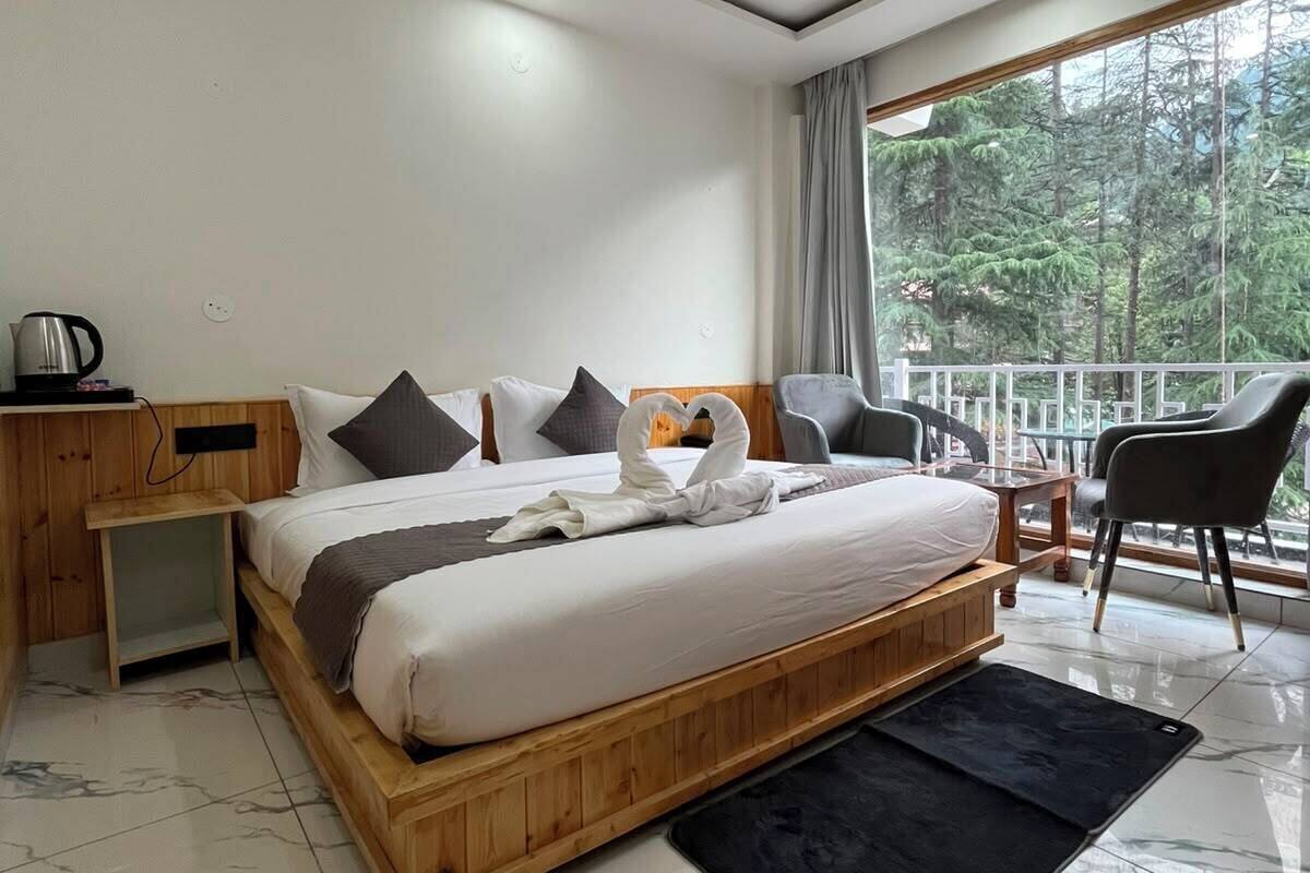 Quarto de hotel moderno com uma cama grande, cabeceira de madeira, uma escrivaninha, uma cadeira e vista para o exterior.