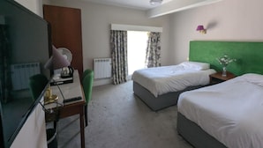 Quarto de hotel com duas camas, uma escrivaninha com cadeira, televisão e janela com cortinas.