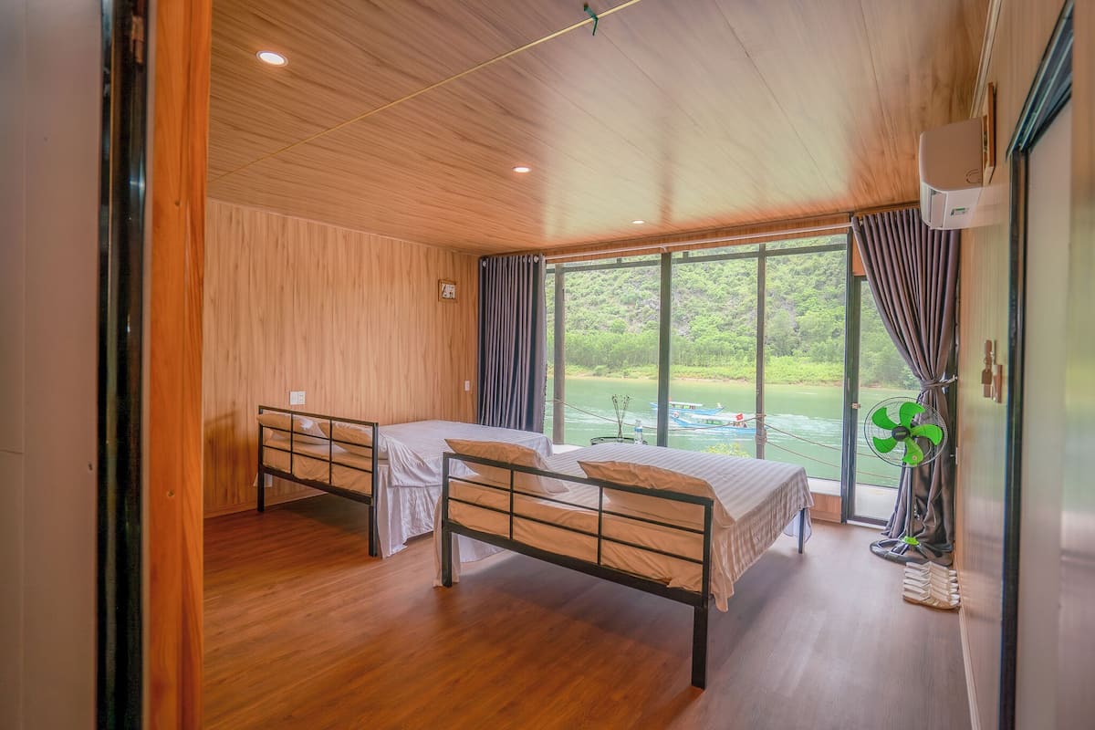 Quarto com duas camas, um ventilador e vista para um rio.