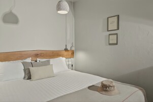 Uma cama bem arrumada com cabeceira de madeira, um chapéu sobre a cama e duas molduras com quadros na parede.