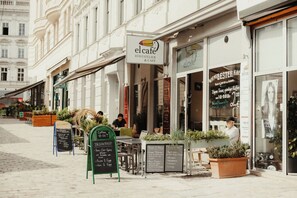 Um café com mesas ao ar livre, uma placa de identificação e um quadro de cardápio.