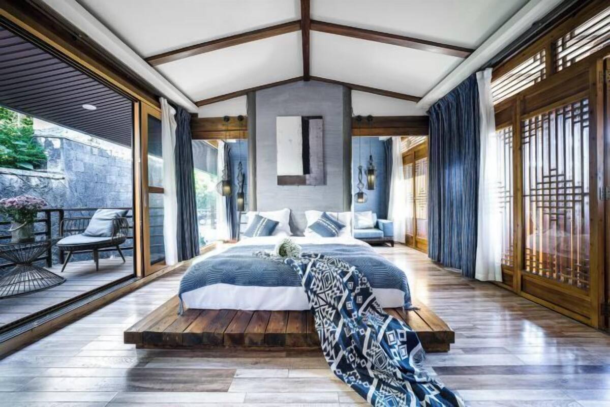 Quarto moderno com uma cama grande, vista para o exterior e varanda com assentos.