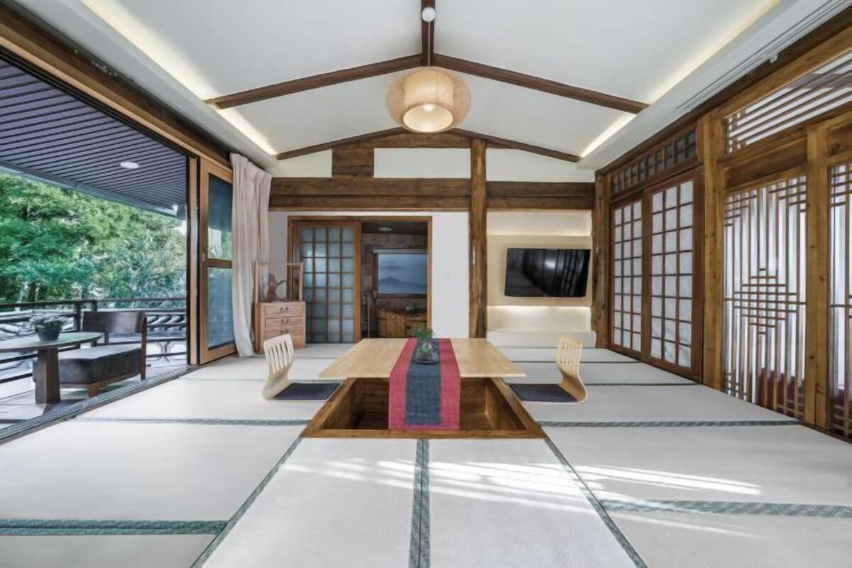Um quarto em estilo japonês tradicional, com tatames, uma mesa de madeira baixa, portas deslizantes e um ventilador de teto.