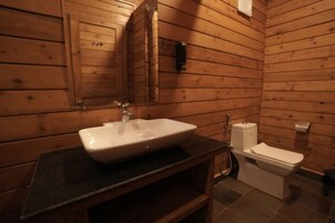 Casa de banho em estilo cabana de madeira, com lavatório, espelho, sanita e dispensador de toalhas.