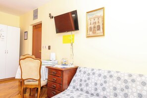 Quarto com cama, escrivaninha, cadeira, televisão presa na parede e um quadro emoldurado.