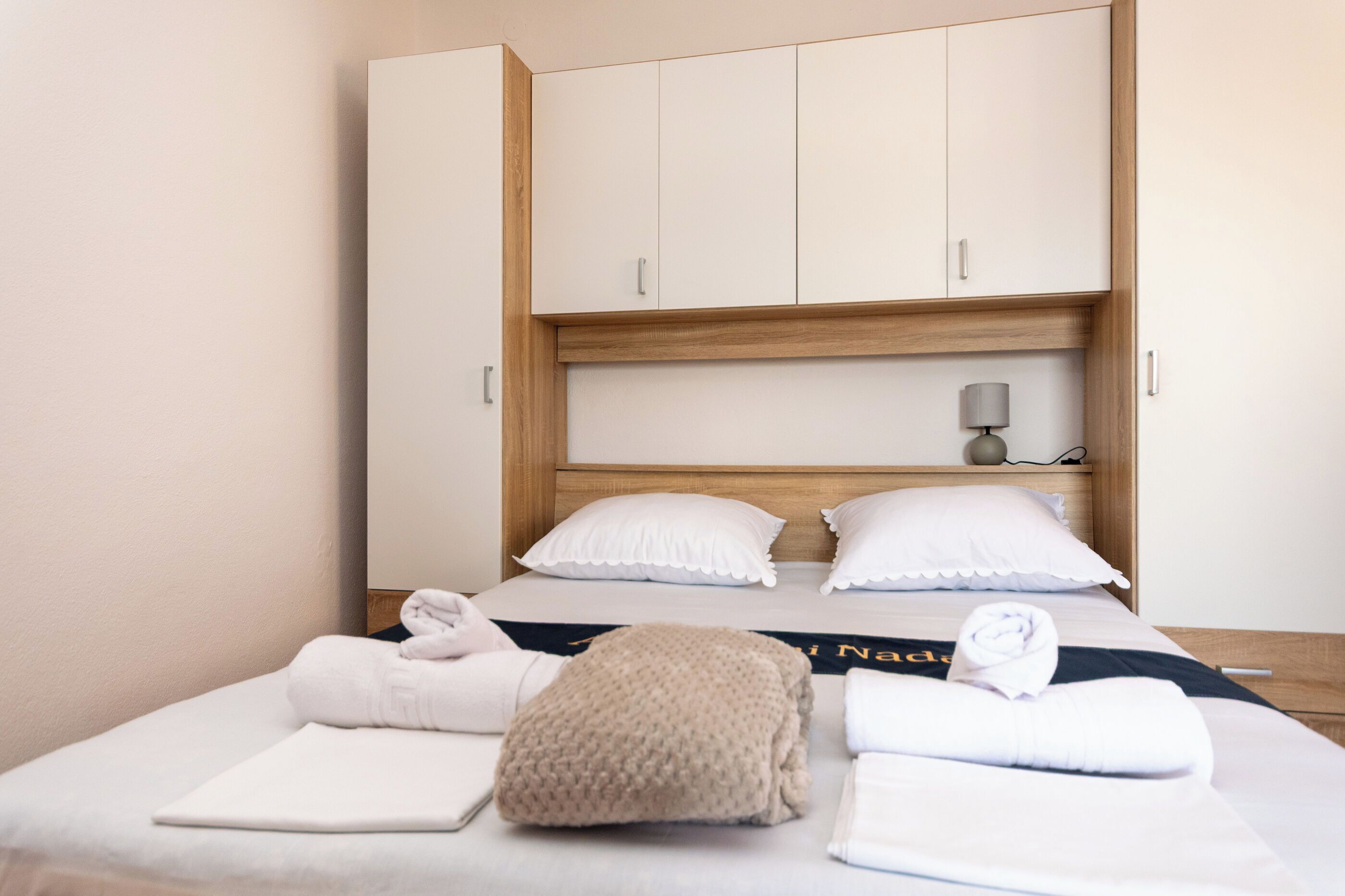 Quarto de hotel com cama, guarda-roupa de madeira e mesa de cabeceira com abajur.