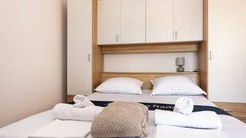 Quarto de hotel com cama, guarda-roupa de madeira e mesa de cabeceira com abajur.
