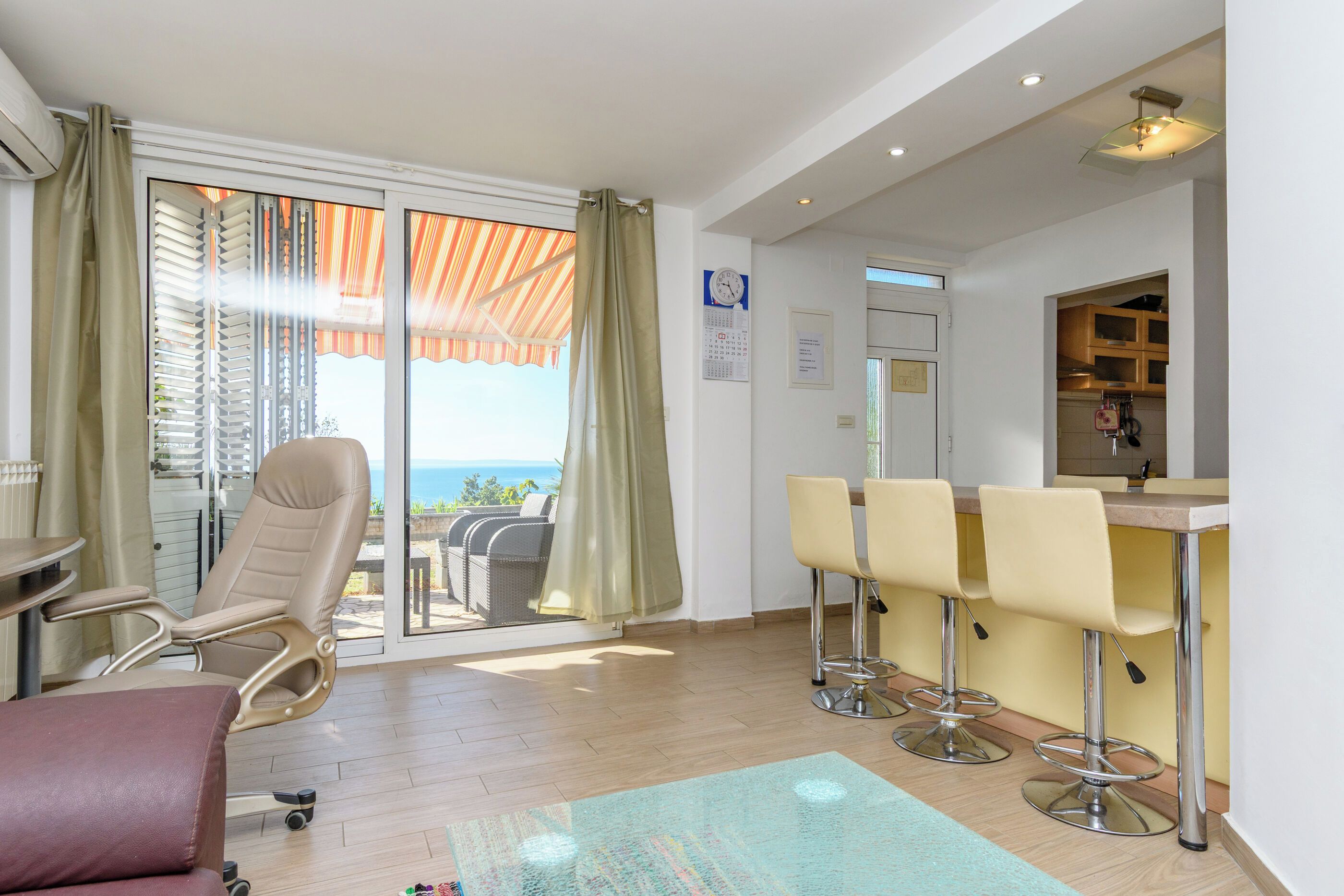 Quarto com vista para o mar, área de bar com banquetas, uma cadeira e uma pequena mesa.