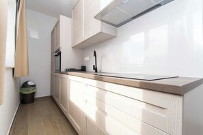 Uma cozinha moderna com armários brancos, coifa de aço inoxidável e lixeira.