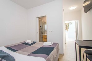 Quarto de hotel com cama, escrivaninha e chuveiro.