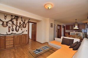 Uma sala de estar com um armário de madeira, uma mesa de centro de vidro, um sofá e um chifre de veado fixado na parede.