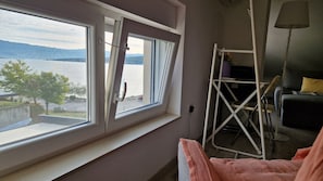 Quarto com janela que dá para um parque de estacionamento e um edifício, uma escada branca e uma cadeira com almofada.